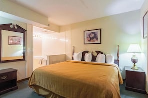 Quarto de hotel com cama, mesa de cabeceira, abajur, espelho e quadro na parede.