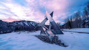 Uma escultura metálica em uma paisagem nevada, com montanhas ao fundo.