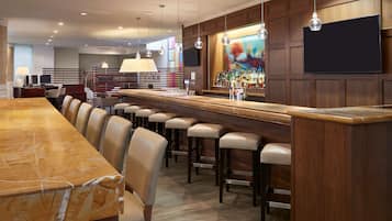 Uma área de bar moderna com bancada de mármore, banquetas e uma variedade de garrafas.