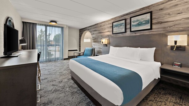 Quarto de hotel moderno com uma cama grande, uma escrivaninha, uma televisão e vista para o exterior pela janela.