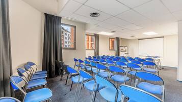 Uma sala de conferências com fileiras de cadeiras azuis, uma lousa e um projetor.