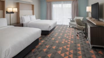 Quarto de hotel com duas camas, uma escrivaninha com televisão, uma cadeira e uma luminária de mesa.