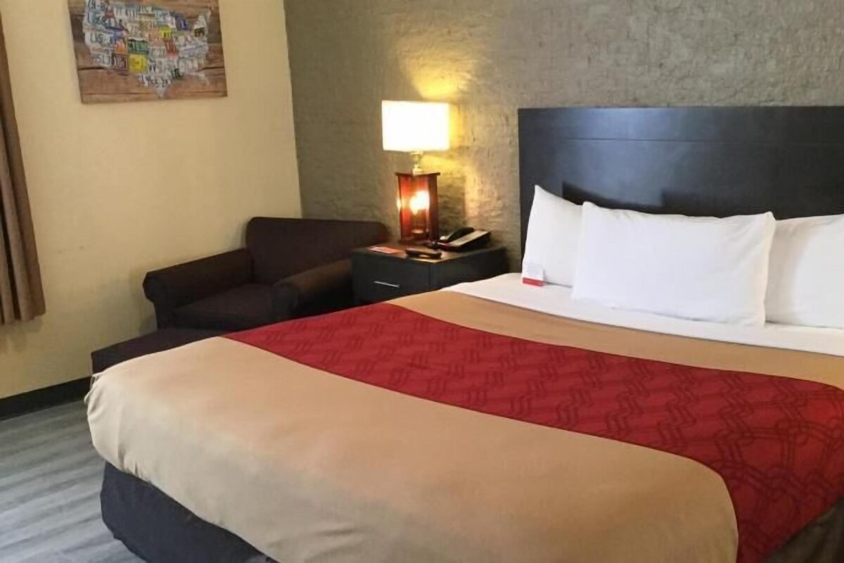Quarto de hotel com uma cama grande, mesa de cabeceira com abajur, um sofá e um mapa na parede.
