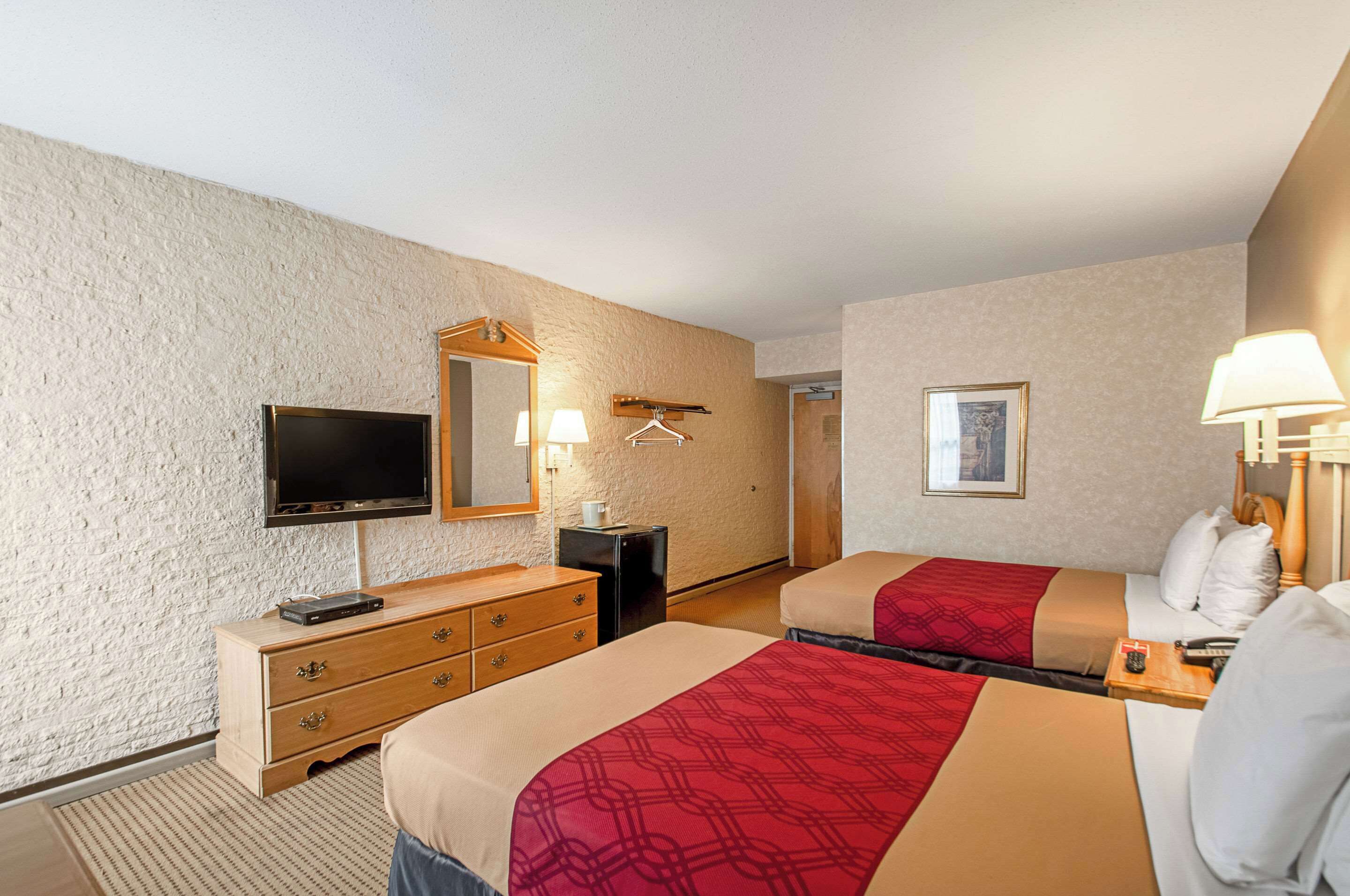 Quarto de hotel com duas camas, televisão, penteadeira, espelho e pequena escrivaninha com abajur.