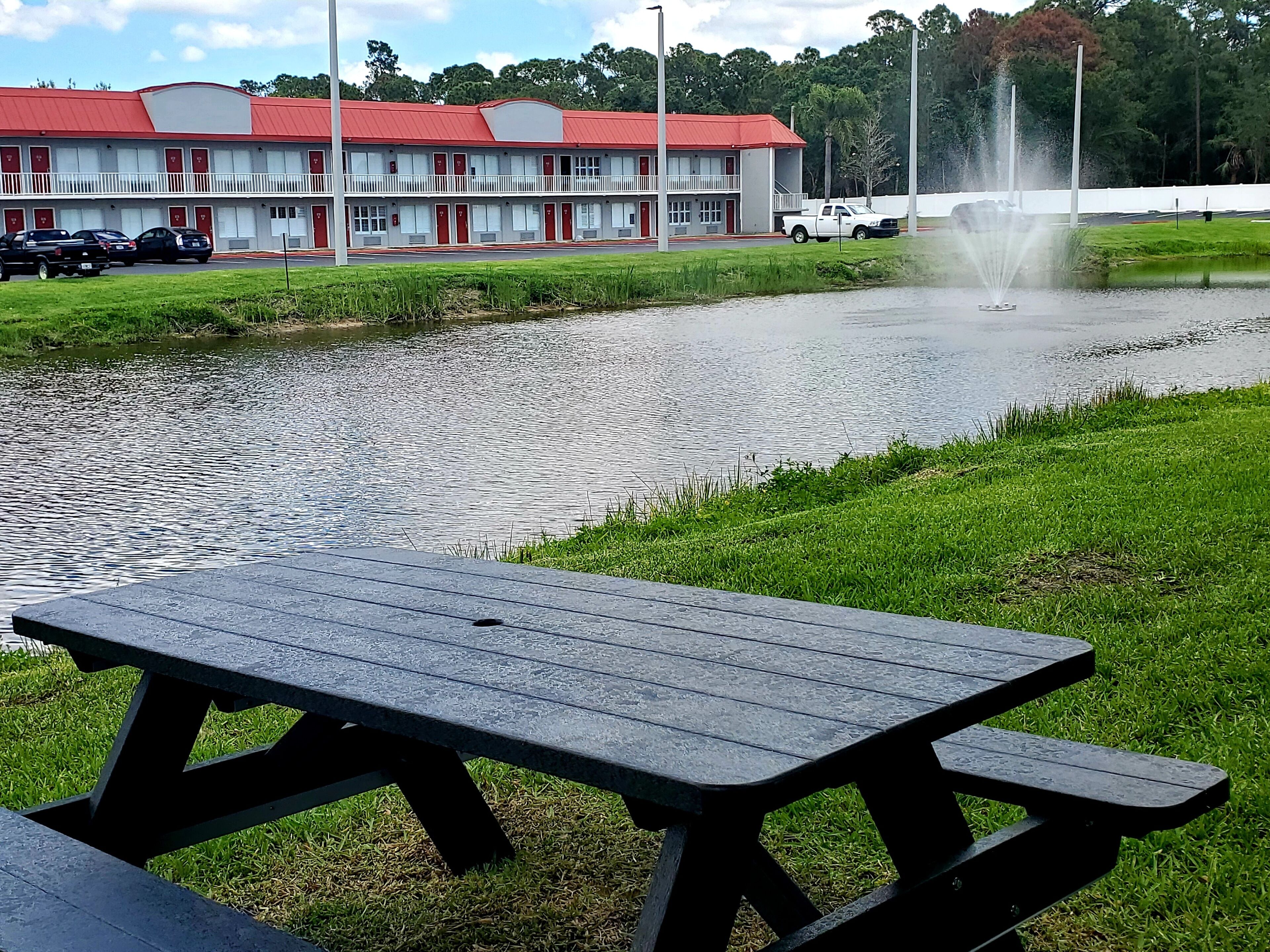 Um motel com telhado vermelho, uma fonte e uma mesa de piquenique em frente.