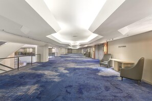 Corredor de hotel com carpete azul, áreas de estar e uma placa na parede com a inscrição 'CALIFORNIA'.