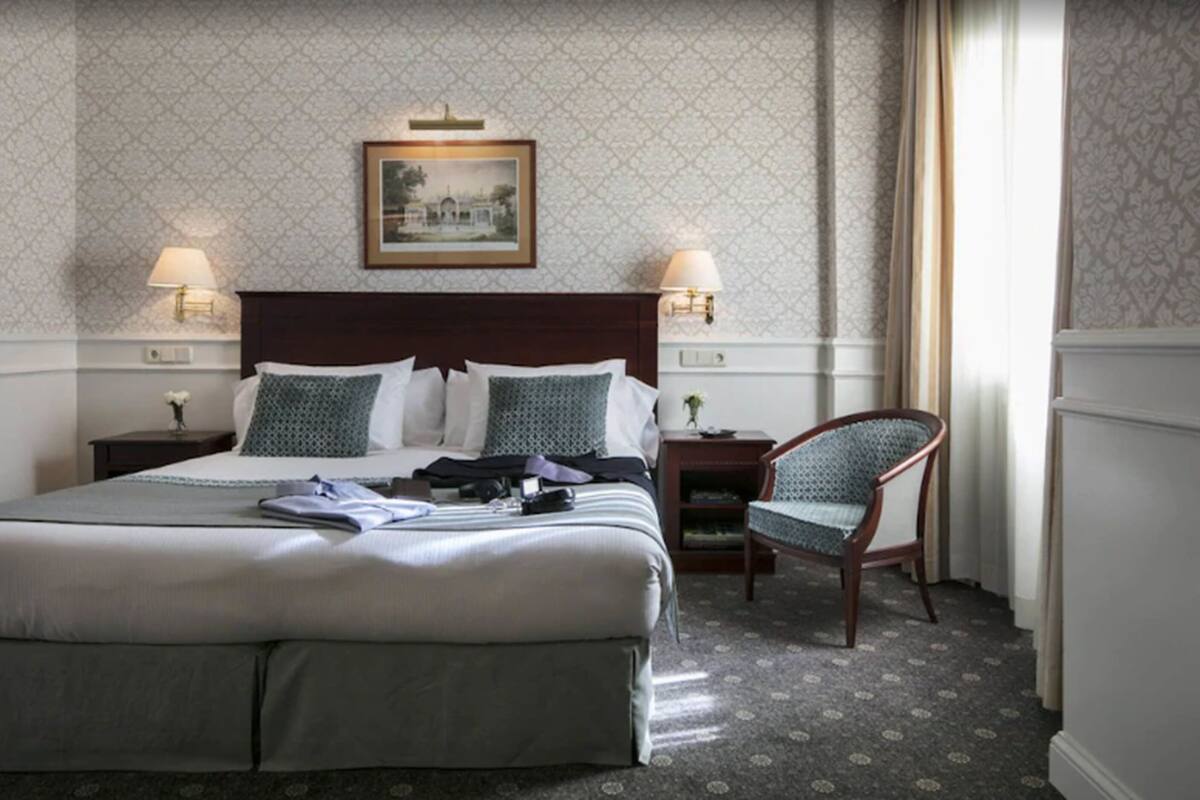 Quarto de hotel bem arrumado com uma cama grande, duas mesas de cabeceira com luminárias, uma cadeira e um quadro na parede.