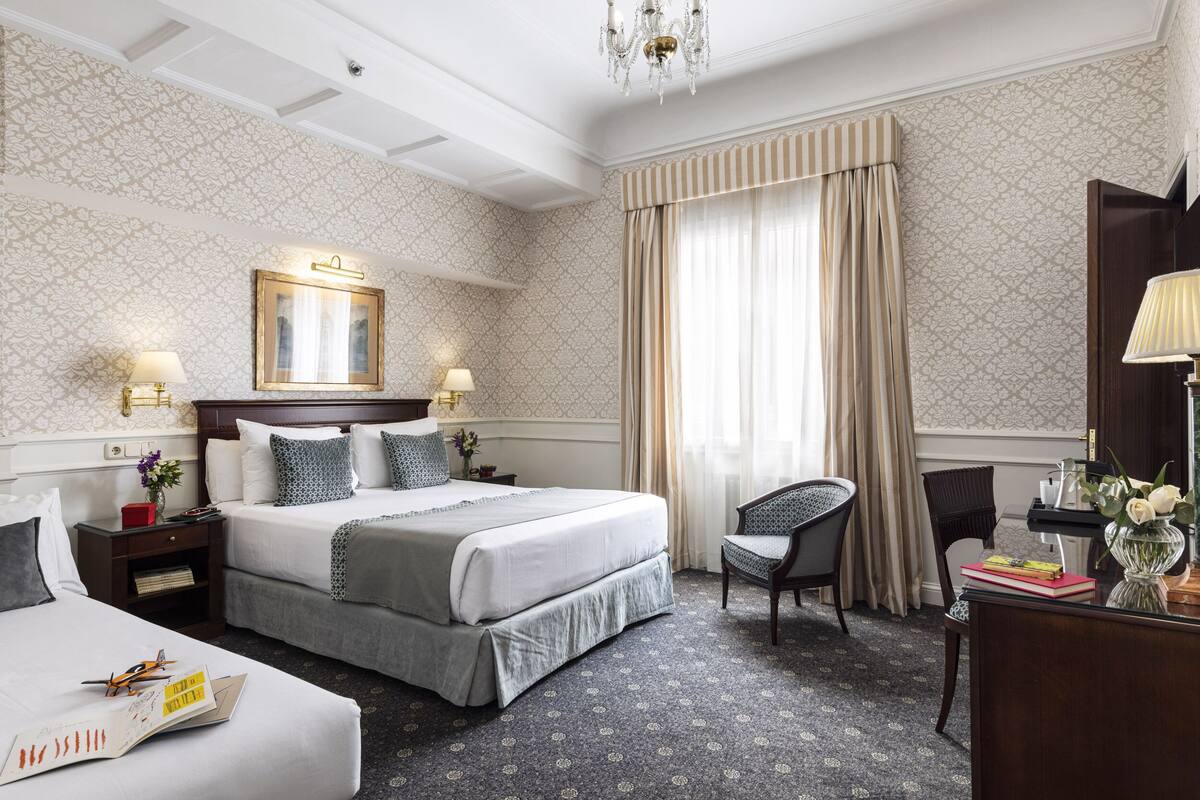 Quarto de hotel com uma cama grande, duas mesas de cabeceira, uma escrivaninha, uma cadeira e um candelabro.