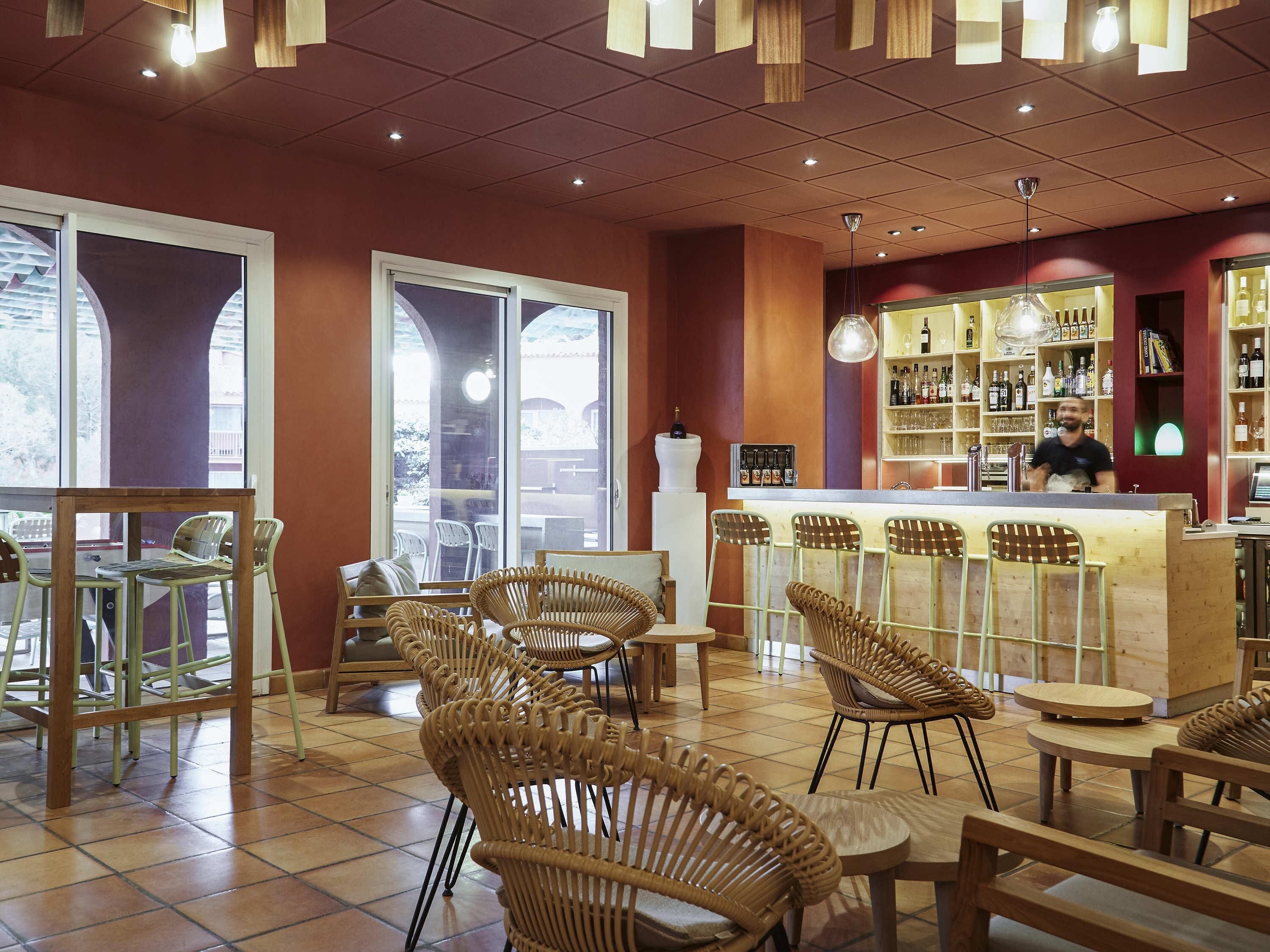 Uma área de bar com cadeiras de vime, balcão e prateleiras com garrafas.