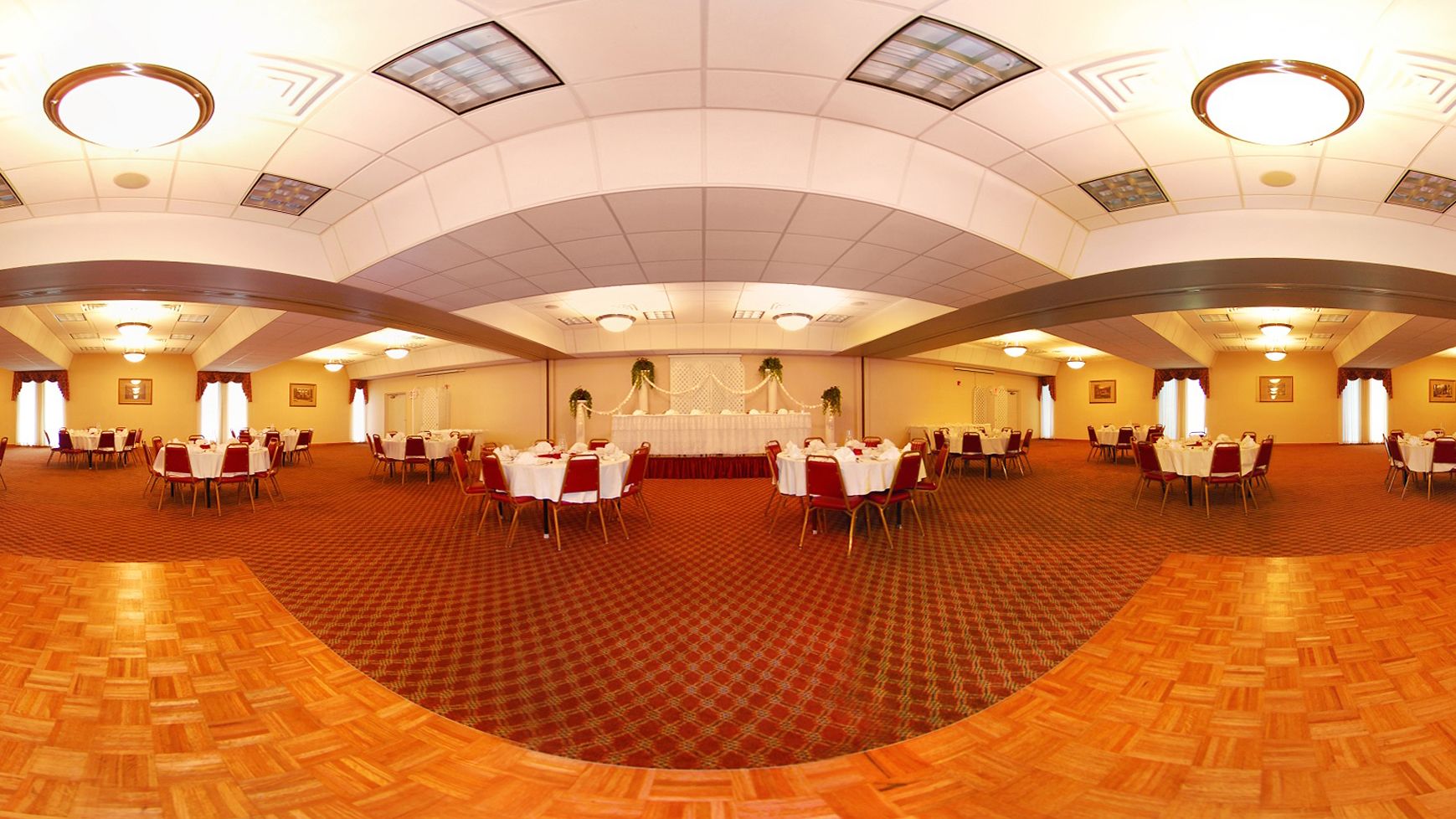 Uma sala de conferências ampla e bem iluminada, com teto alto, várias mesas dispostas para refeições e uma área de palco central.