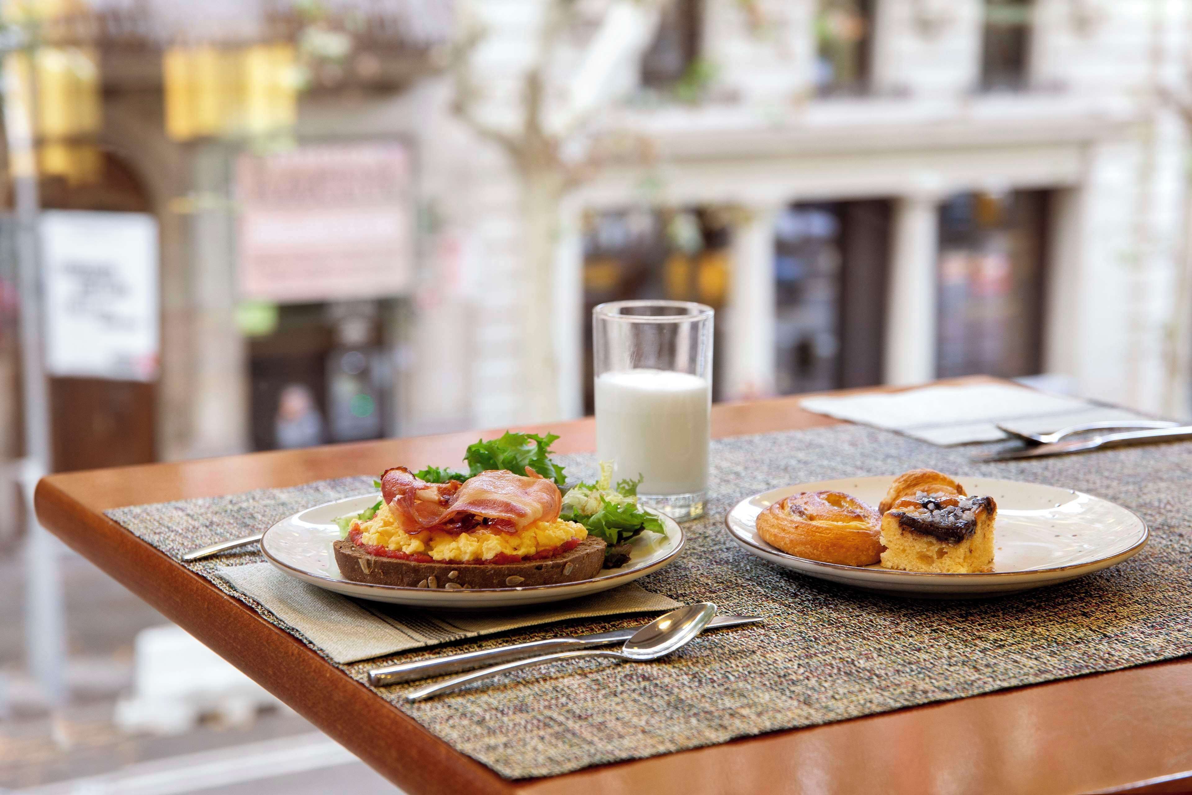 Uma mesa posta para o café da manhã, com torradas cobertas de ovos e bacon, um copo de leite e um muffin.