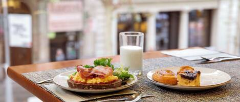 Uma mesa posta para o café da manhã, com torradas cobertas de ovos e bacon, um copo de leite e um muffin.