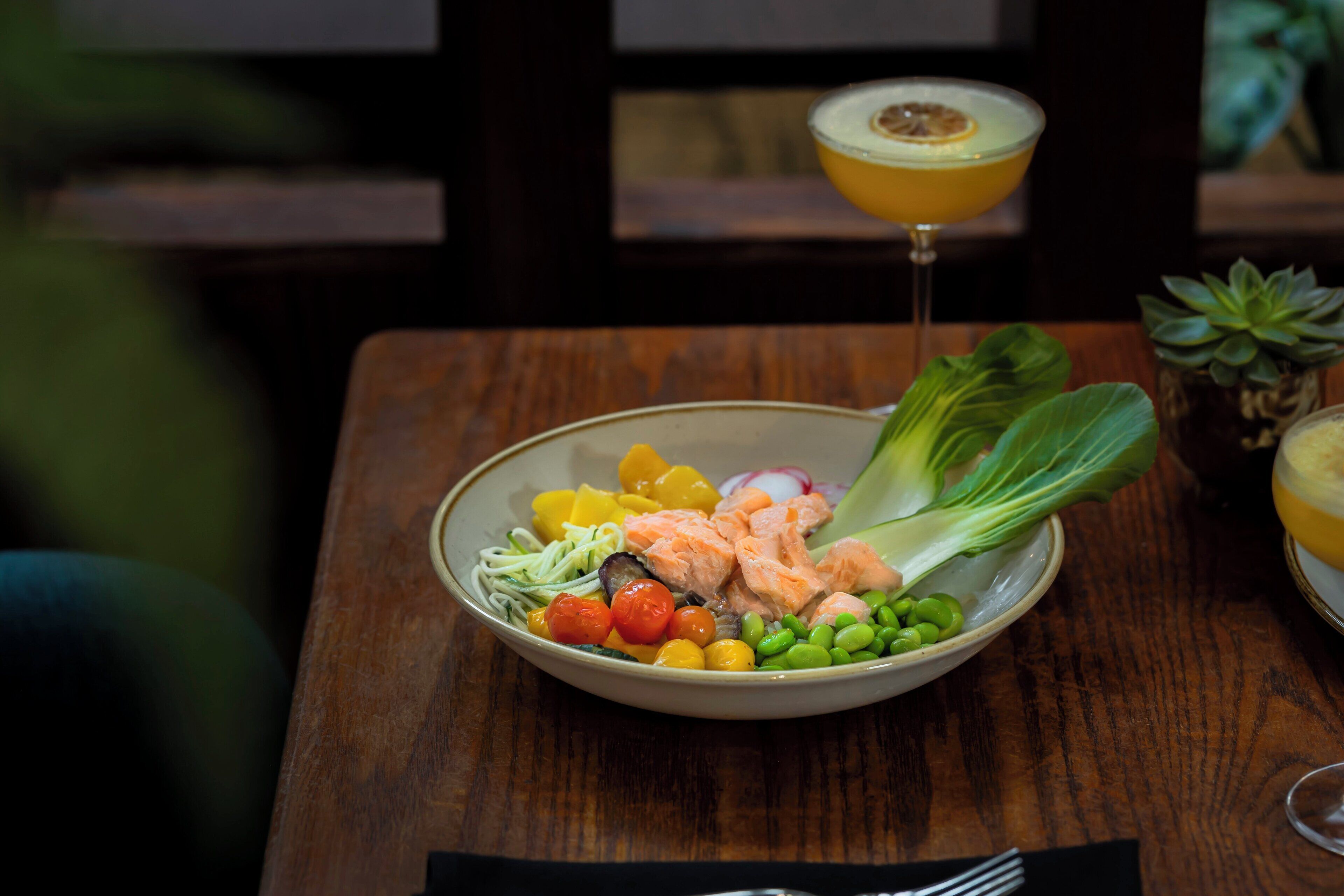 Uma tigela de comida com legumes e salmão sobre uma mesa de madeira.