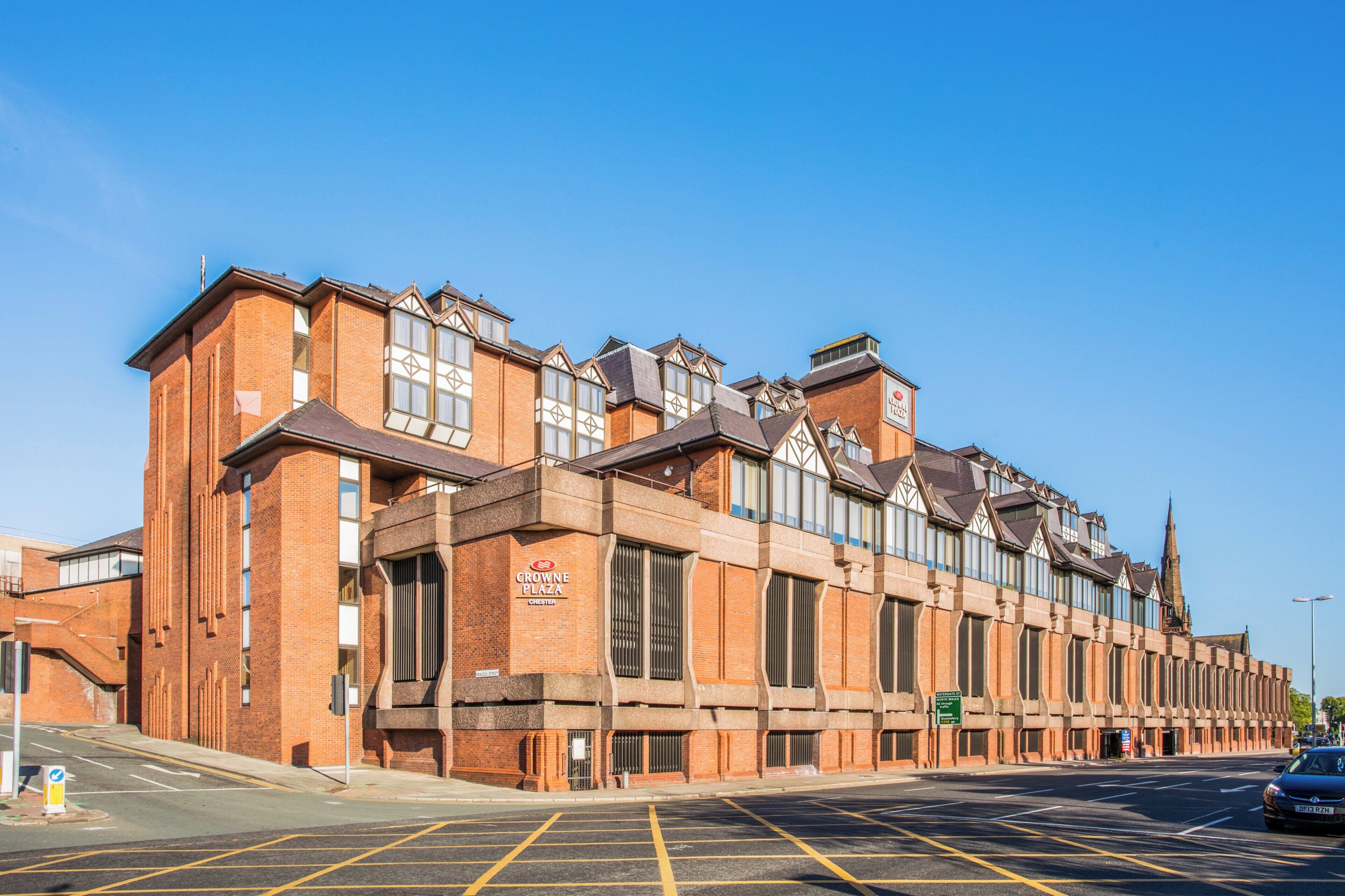 Um edifício grande de tijolos, com várias janelas e uma placa com a inscrição 'Crown Plaza Chester'.