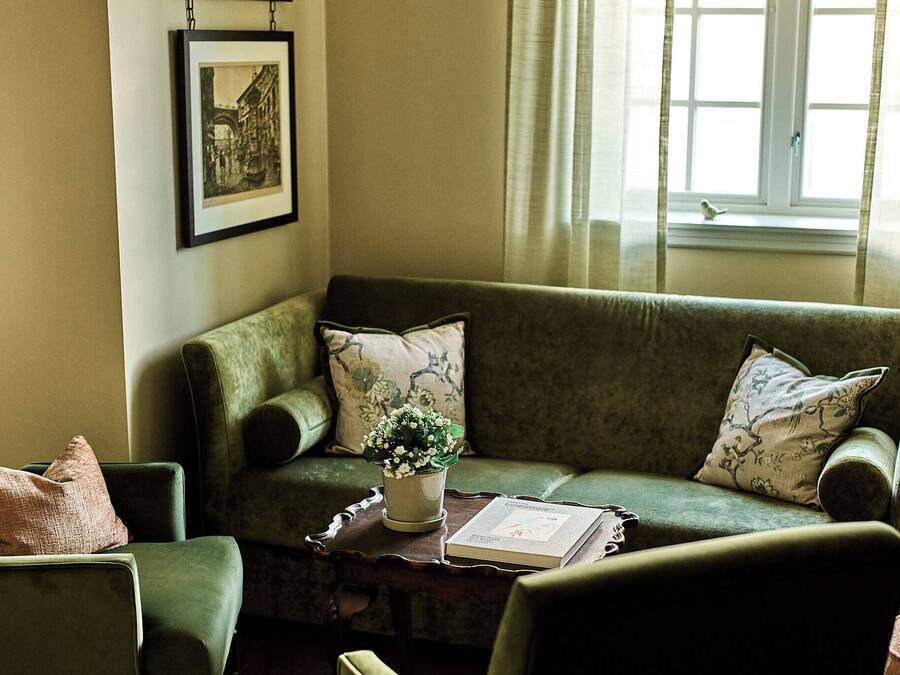 Uma sala de estar acolhedora com um sofá verde, uma mesinha com um livro e uma planta, e um quadro na parede.