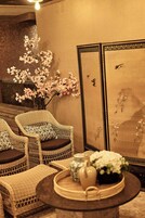 Quarto com mobiliário de vime, um vaso com flores e uma obra de arte emoldurada com pássaros.