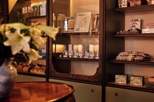 Quarto de hotel com minibar, um vaso com flores e uma estante com livros e garrafas.