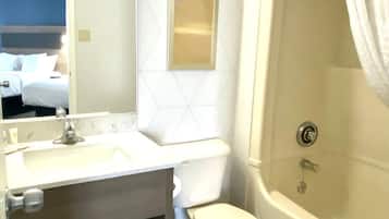 Casa de banho com lavatório, sanita e banheira. Existe um contentor azul de reciclagem junto ao lavatório.