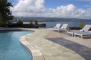 Uma área de piscina com espreguiçadeiras e vista para um lago e montanhas.