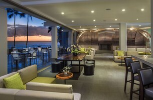 Uma área de estar moderna com uma grande mesa de madeira, sofás e cadeiras, vista para o mar e um design de parede curva único.