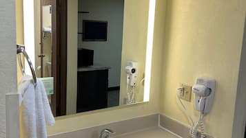 Casa de banho com lavatório, espelho, porta-toalhas, secador de cabelo e um cesto de lixo.