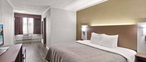 Quarto de hotel com cama, mesas de cabeceira, escrivaninha e janela com cortinas.