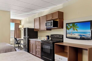 Quarto de hotel com cozinha compacta, incluindo micro-ondas, fogão, frigorífico e televisão de ecrã plano fixada na parede.