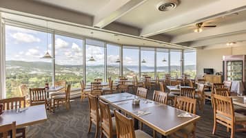 Uma sala de jantar com grandes janelas que oferecem uma vista panorâmica do campo. Mesas e cadeiras dispostas para refeições.