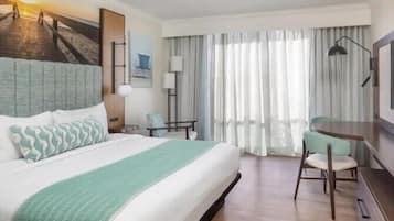 Quarto de hotel com uma cama grande, uma escrivaninha, uma cadeira, um abajur e um quadro na parede.
