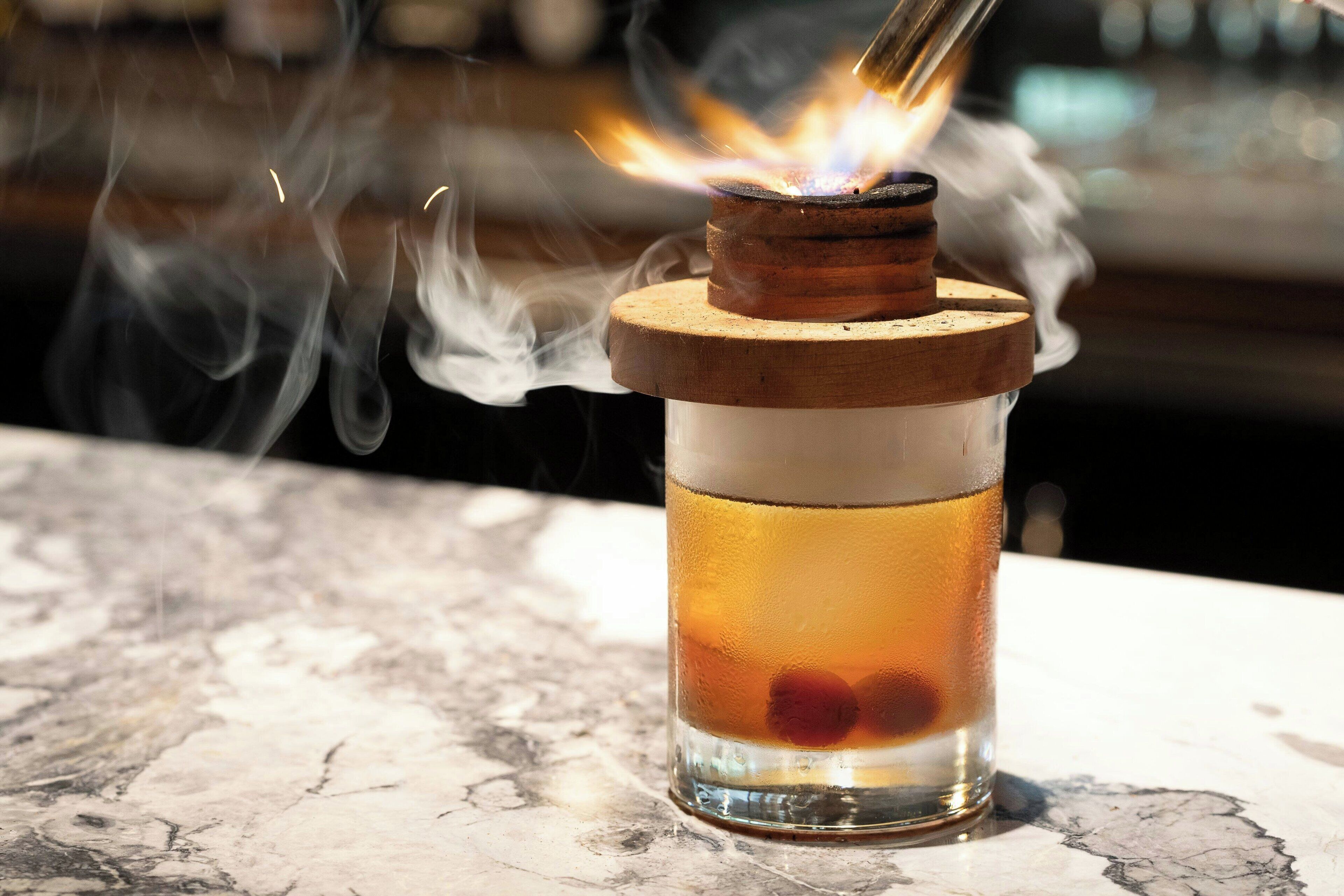 Um copo com tampa de madeira e uma vela acesa no interior, sobre uma superfície de mármore.