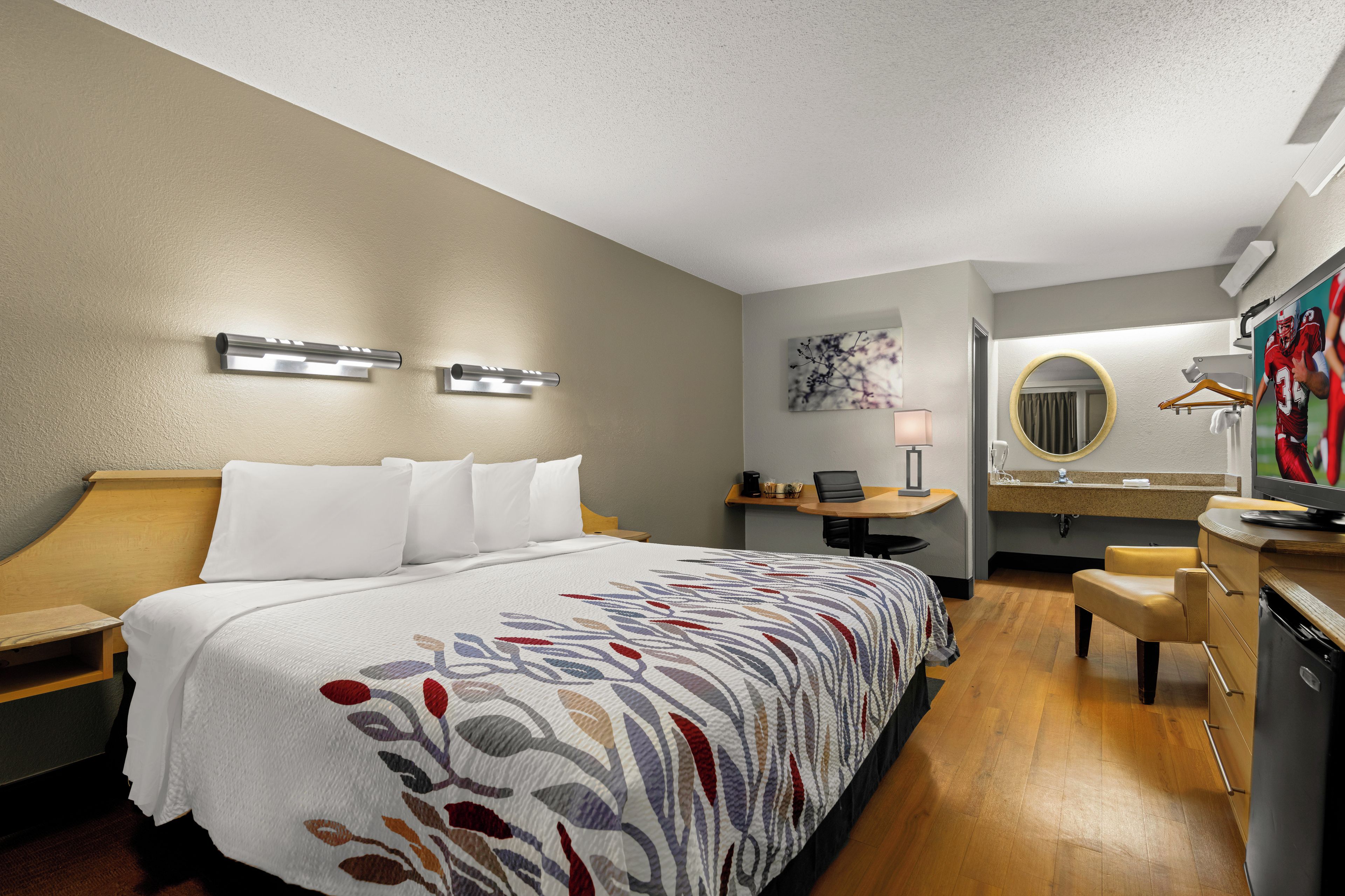 Quarto de hotel com uma cama grande, escrivaninha com computador, cadeira, espelho e televisão.
