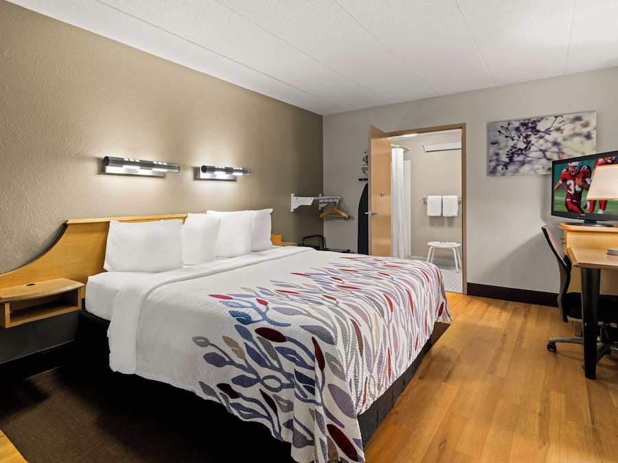 Quarto de hotel com cama, mesas de cabeceira, escrivaninha, cadeira, televisão e um quadro na parede.