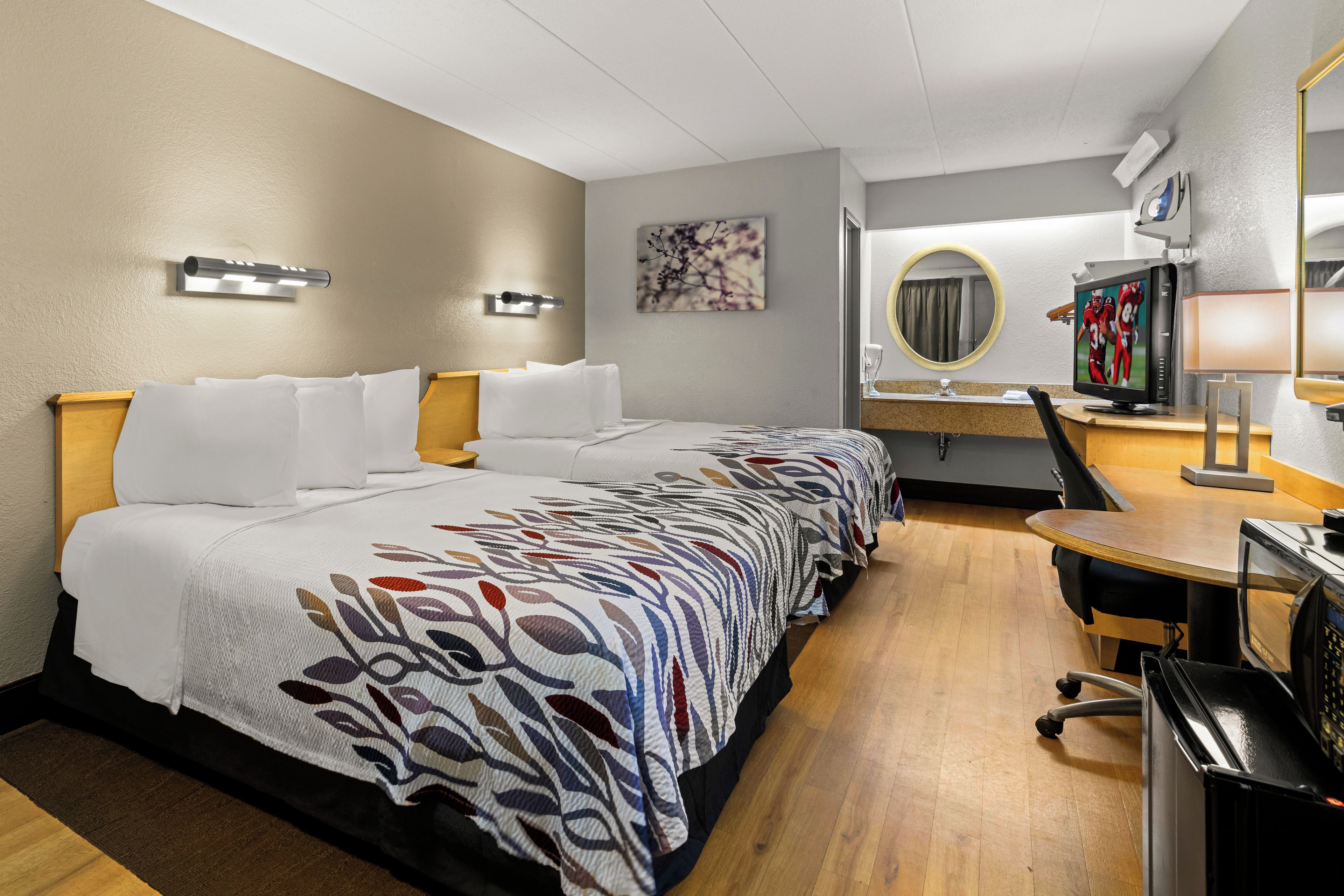 Quarto de hotel com uma cama grande, uma escrivaninha com computador, televisão e espelho.