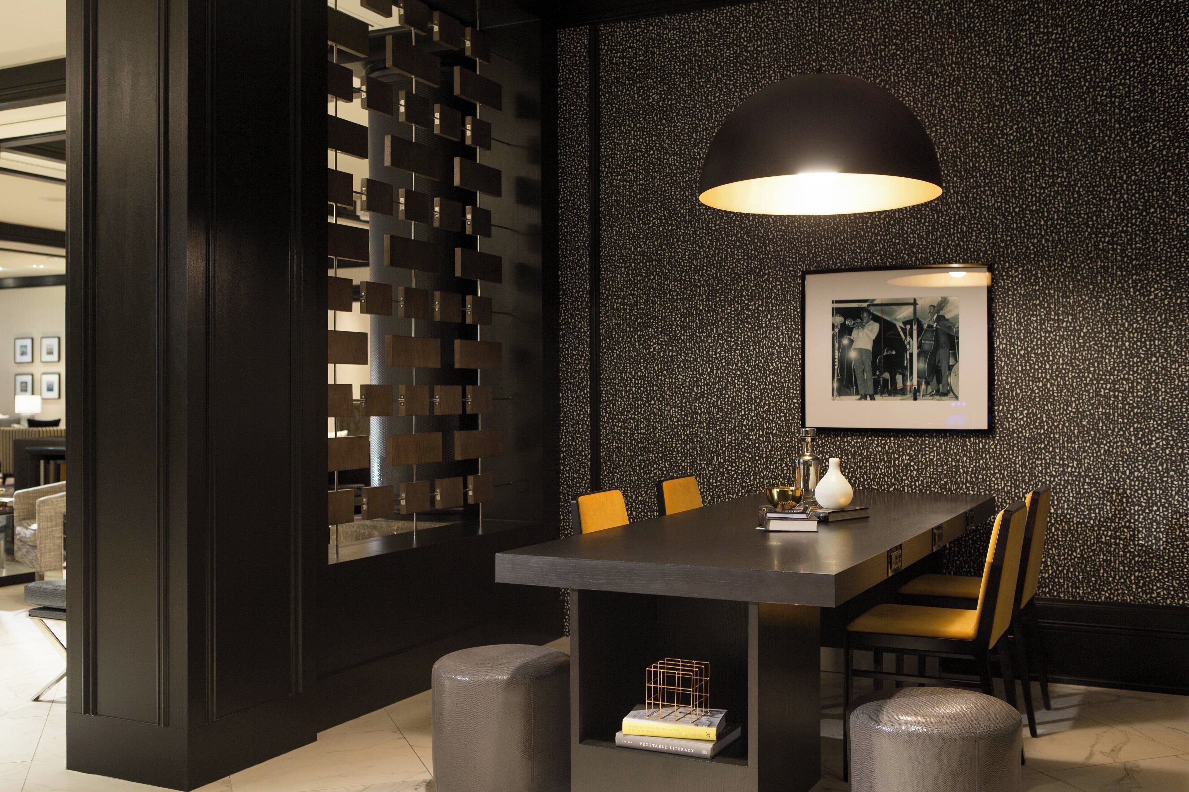 Uma sala de jantar moderna com mesa de madeira escura, cadeiras e uma luminária pendente.
