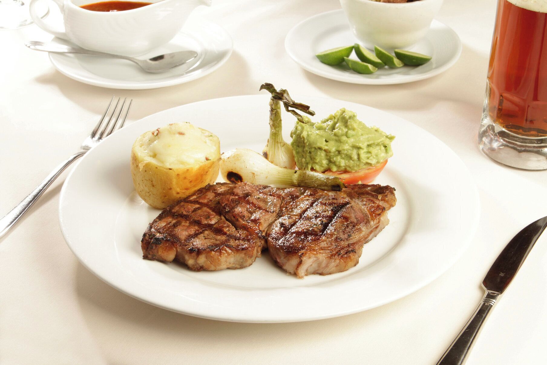 Prato com bife grelhado, batatas assadas, fatia de tomate e guacamole.