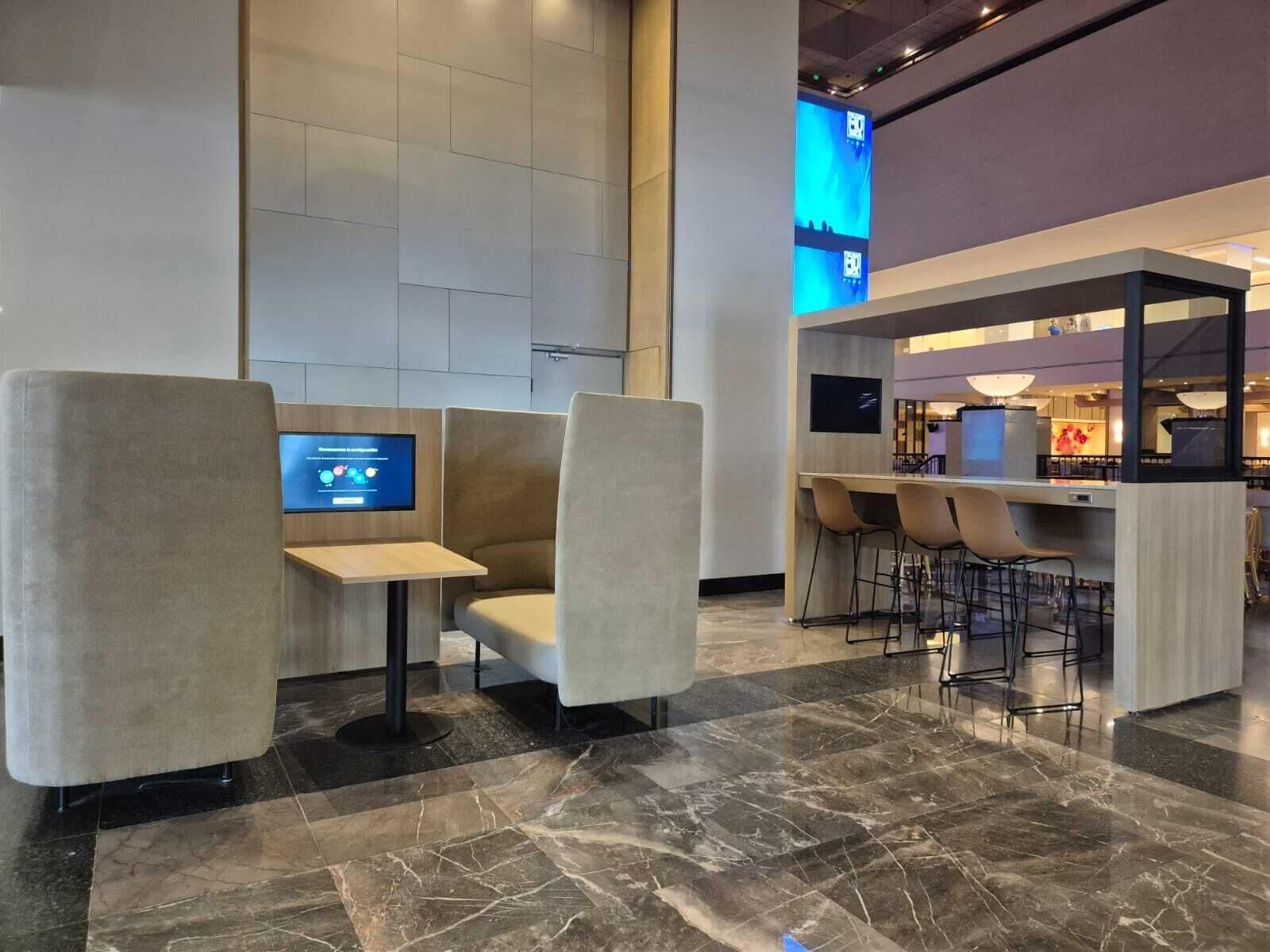 Um lobby de hotel moderno com áreas de estar, um balcão de recepção e um painel digital.