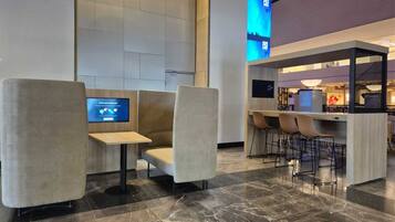 Um lobby de hotel moderno com áreas de estar, um balcão de recepção e um painel digital.