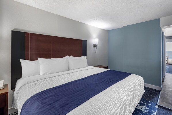 Quarto de hotel com uma cama grande, cabeceira, mesa de cabeceira, luminária na parede e vista para o exterior.