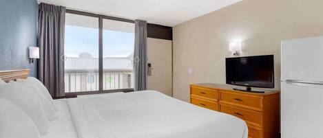 Quarto de hotel com uma cama grande, televisão, cómoda e frigorífico.