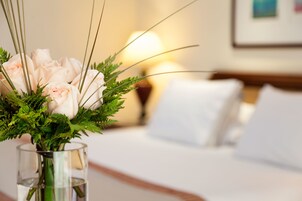 Quarto de hotel com cama, mesa de cabeceira com um vaso de flores e uma lumin ária.