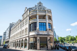 Um edifício histórico com café e teatro no andar térreo, com grandes janelas e estilo arquitetônico clássico.