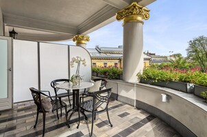 Um terraço com mesa redonda e cadeiras, um pilar decorativo e vista para edifícios e plantas.