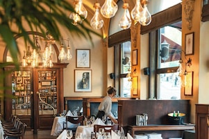 Interior de restaurante com luminárias pendentes, obras de arte emolduradas nas paredes e uma pessoa sentada à mesa.