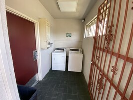 Uma lavanderia com duas máquinas de lavar, um aviso com os horários de funcionamento para hóspedes e uma câmera de segurança.
