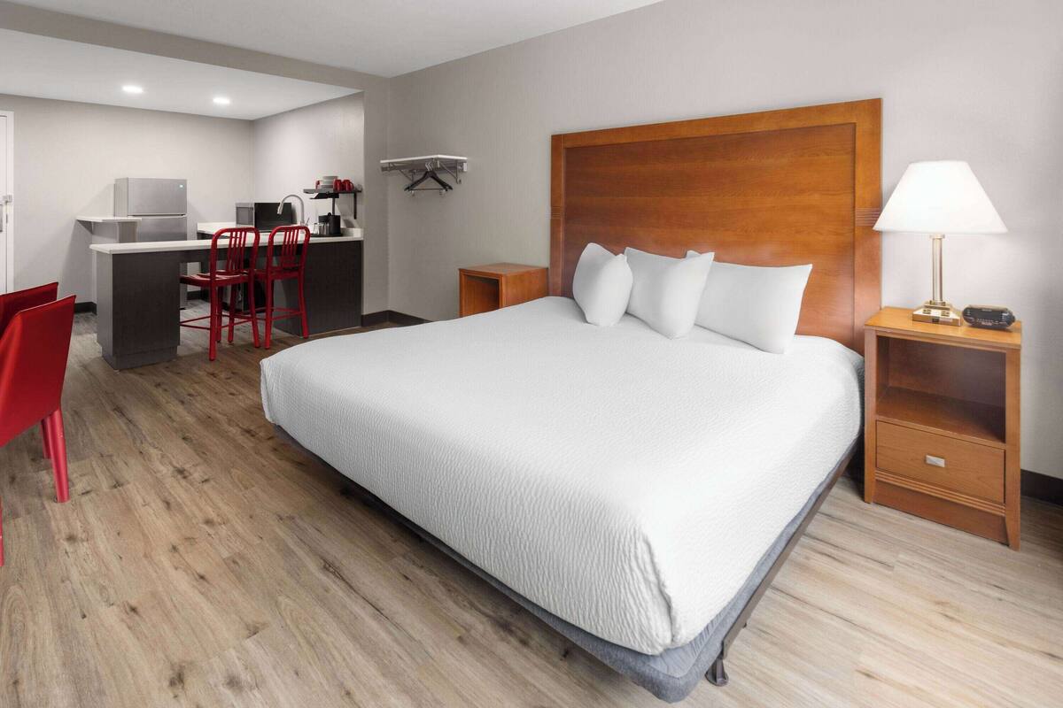 Quarto de hotel com uma cama grande, uma mesa com cadeira, uma mesinha e uma luminária.