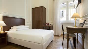 Quarto de hotel com cama, escrivaninha, cadeira, guarda-roupa e janela com cortinas.