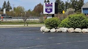 Placa da Knights Inn num parque de estacionamento, com sinalização de limite de peso, rodeada por vegetação e árvores.