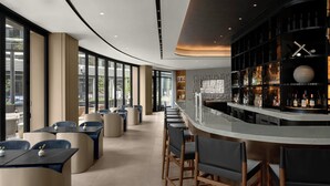Uma área de bar moderna com balcão curvo, assentos com encosto alto e uma grande janela que oferece vista para o exterior.