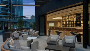 Uma área de estar moderna ao ar livre, com sofás, cadeiras e mesas, com vista para a paisagem urbana.