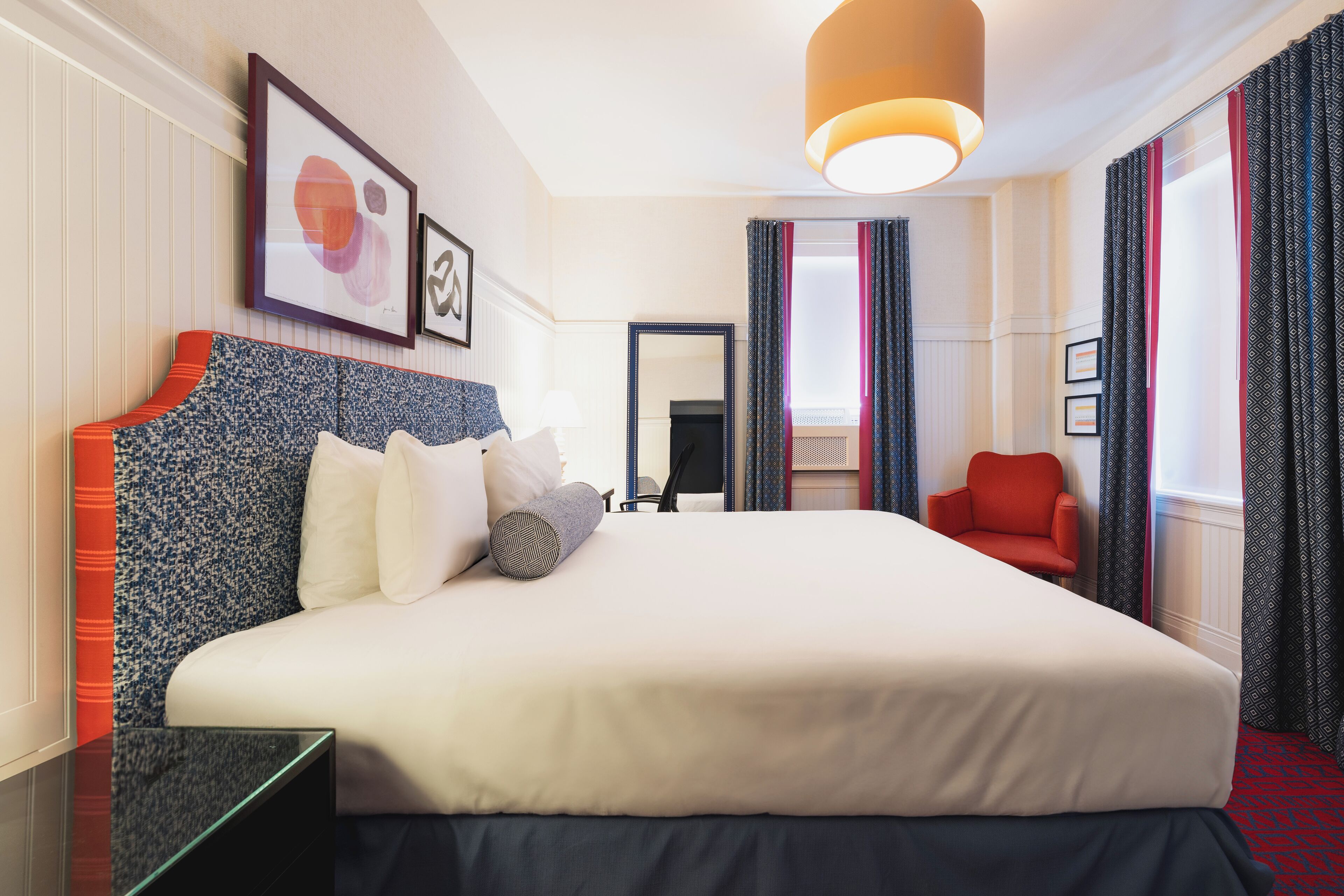 Quarto de hotel com uma cama grande, uma poltrona vermelha e um espelho na parede.